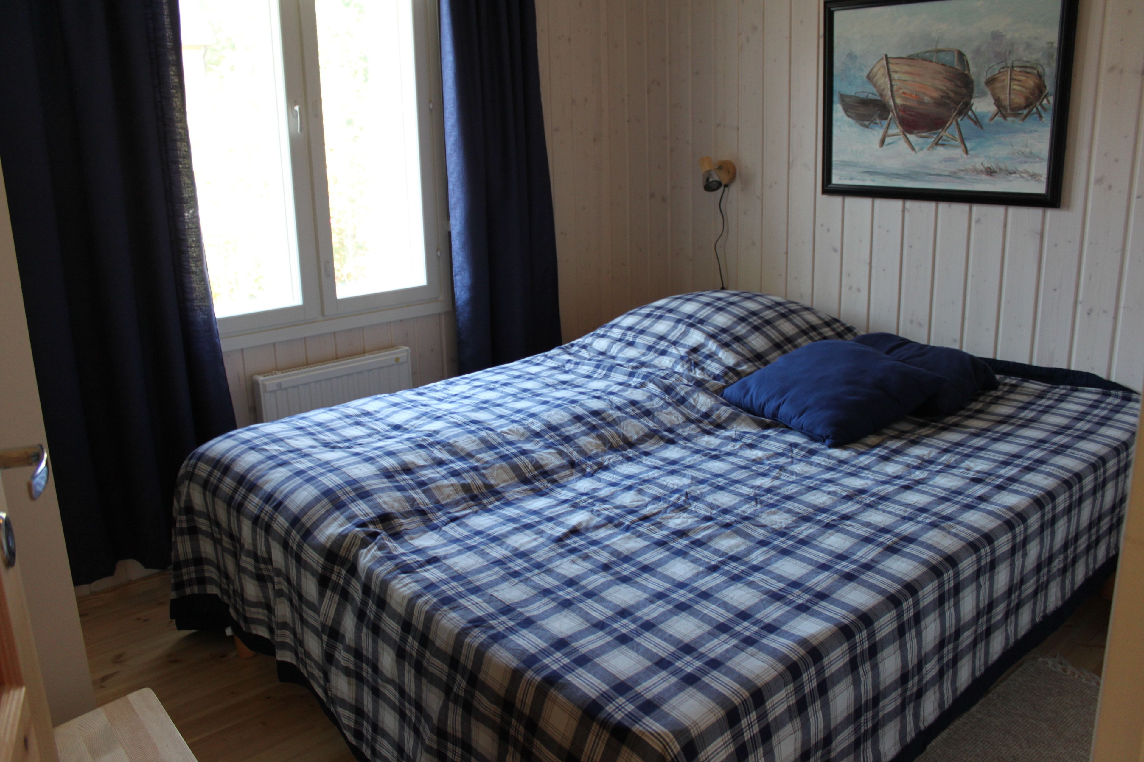 Um quarto com cama, janela com cortinas, radiador e um quadro na parede.