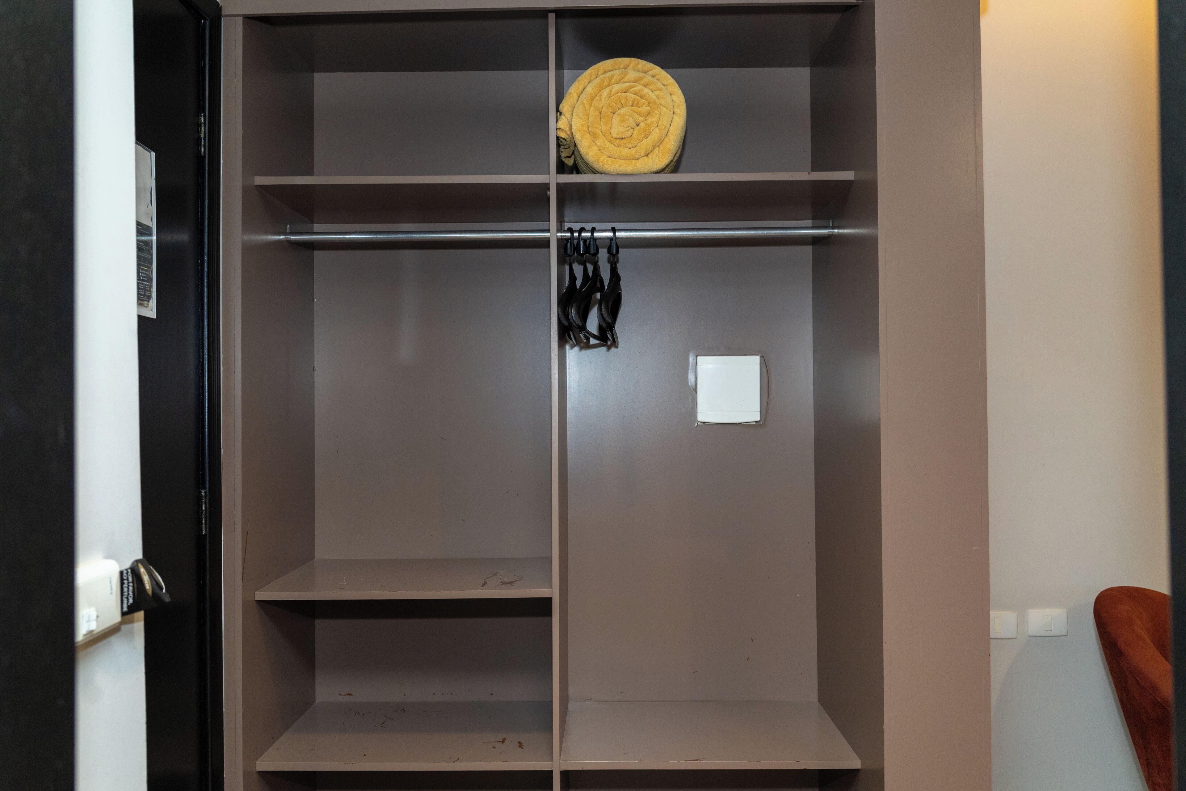 Guarda-roupa fechado com três prateleiras, uma barra para pendurar roupas e um pequeno interruptor branco no lado direito.