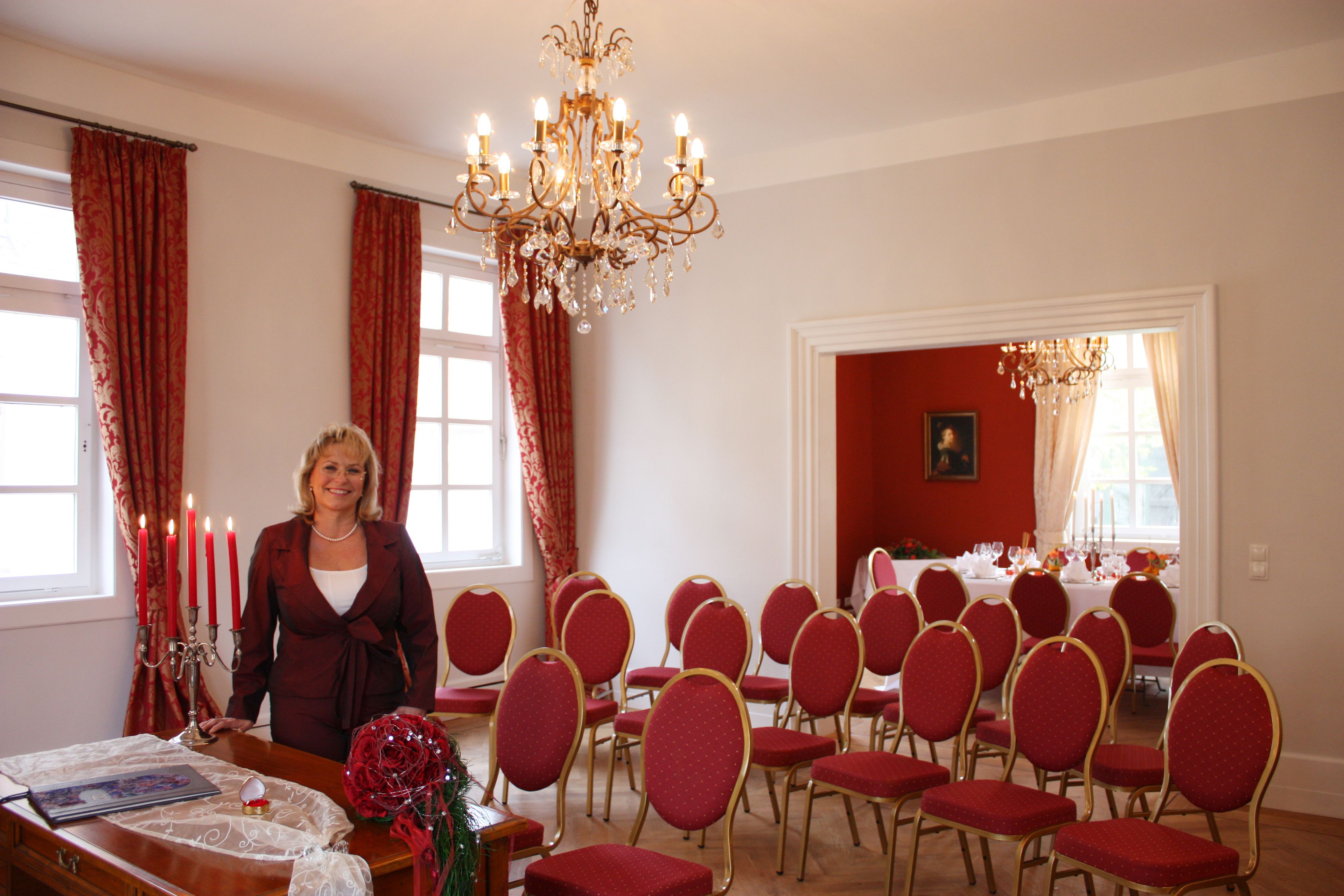 Um quarto com um candelabro, cortinas vermelhas e uma mesa posta para refeição.