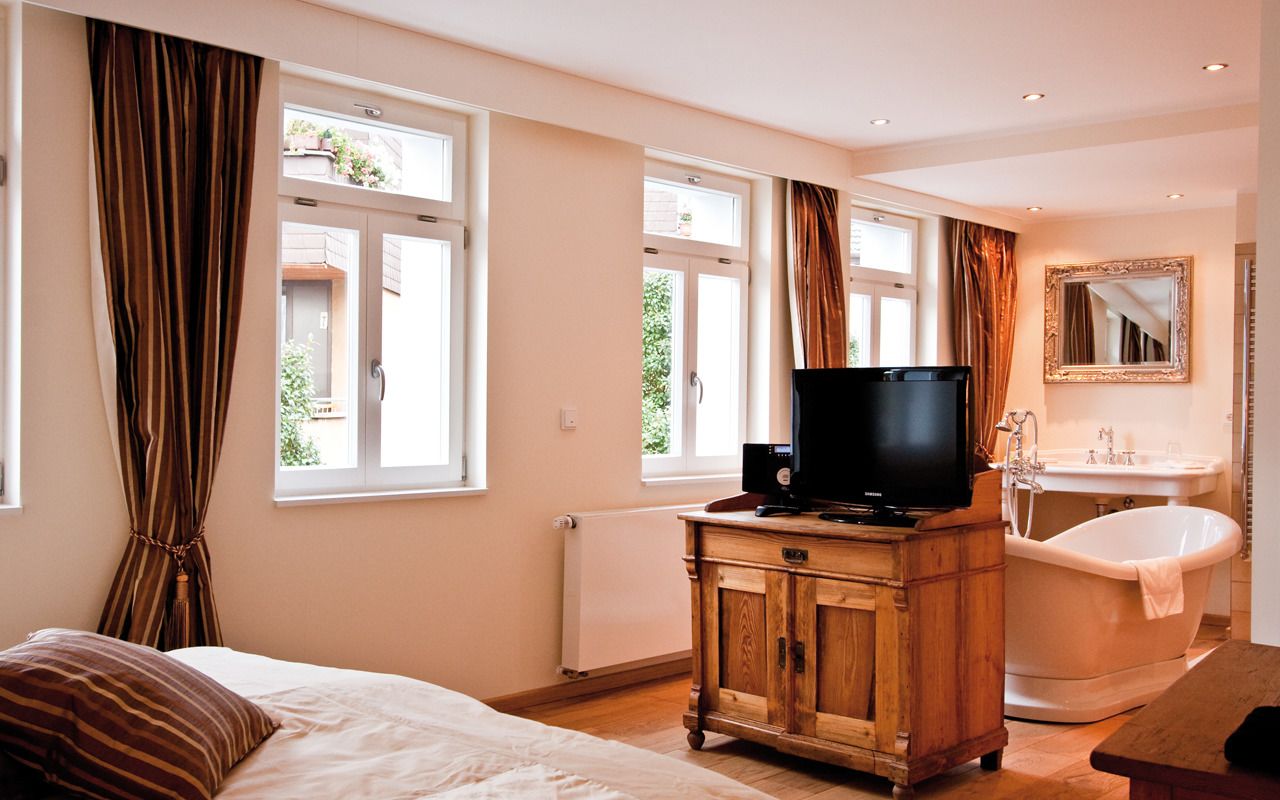 Quarto com cama, penteadeira de madeira, televisão, banheira e janela com cortinas.