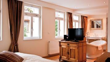 Quarto com cama, penteadeira de madeira, televisão, banheira e janela com cortinas.