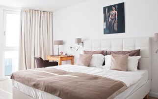 Quarto de hotel com cama grande, escrivaninha, duas luminárias e janela com cortinas.