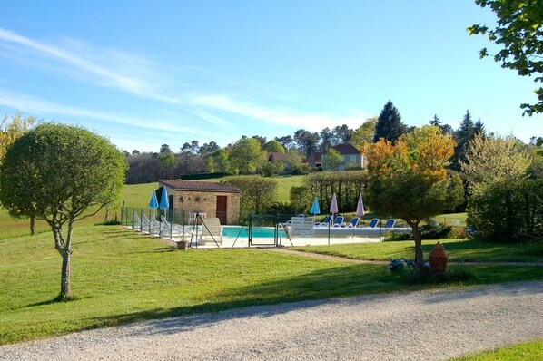 Uma área de piscina com um pequeno edifício, um deck cercado e cadeiras de descanso.