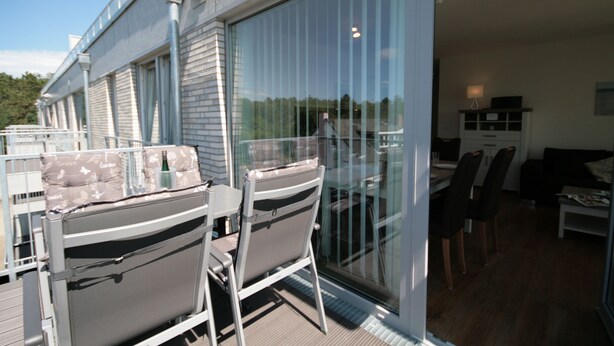 Uma varanda com mesa e cadeiras, uma porta de correr de vidro e vista para o exterior.