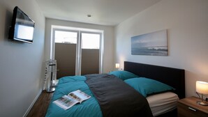 Quarto com cama, mesa de cabeceira, luminária, televisão e janela com persianas.