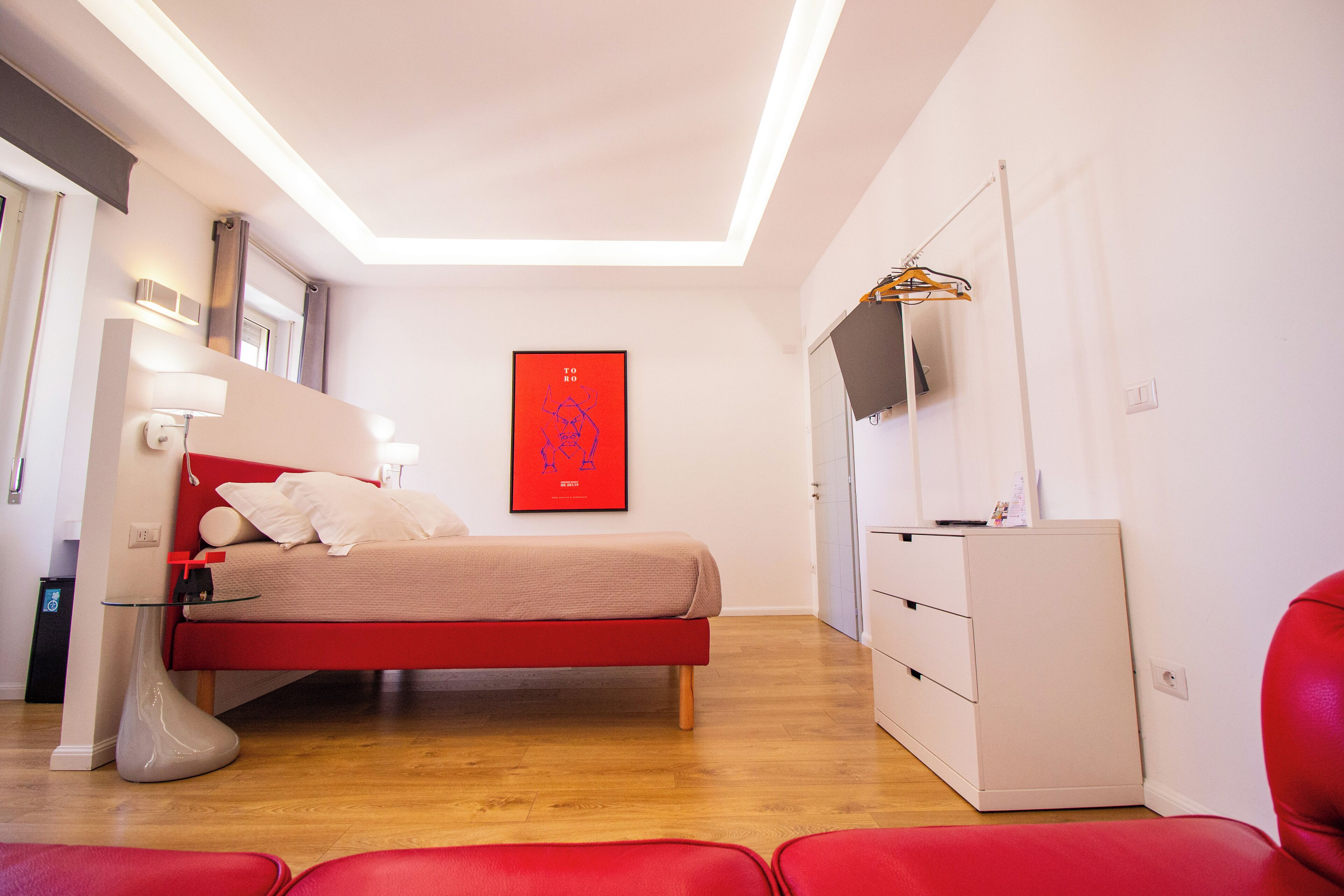 Quarto moderno com cama, mesa de cabeceira e televisão em suporte.