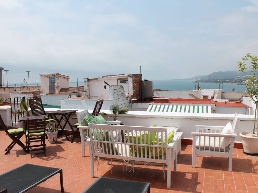 Terraço no telhado com mobiliário externo, plantas em vasos e vista para o mar.