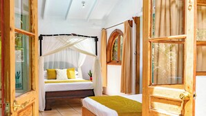 Quarto com cama, mesa de cabeceira, janela com cortinas e porta de madeira.