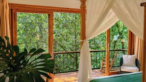 Quarto com uma janela grande, uma cama, uma cadeira e uma planta.