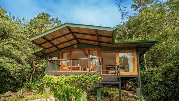 Uma cabana de madeira com varanda, rodeada por vegetação exuberante.