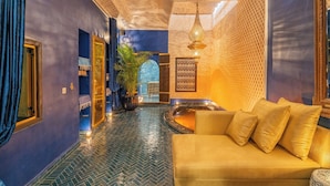 Um interior luxuoso com piso em padrão herringbone, um sofá com almofadas, uma parede decorativa e um lustre.