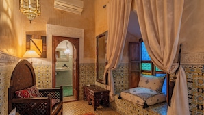 Quarto tradicional marroquino com uma cama, um espaço de estar e uma mesinha com uma luminária.