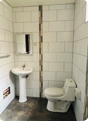 Um banheiro pequeno com azulejos brancos, pia de pedestal, vaso sanitário e espelho.