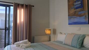 Quarto de hotel com cama, um quadro na parede, uma luminária e vista pela janela.