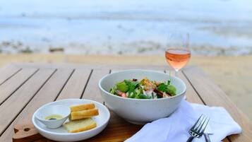 Uma mesa de madeira com uma salada numa tigela, um copo de vinho e um pequeno recipiente com molho.