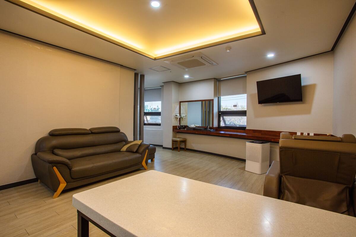 Quarto de hotel moderno com sofá, uma pequena mesa, televisão fixada na parede e janela com vista para o exterior.