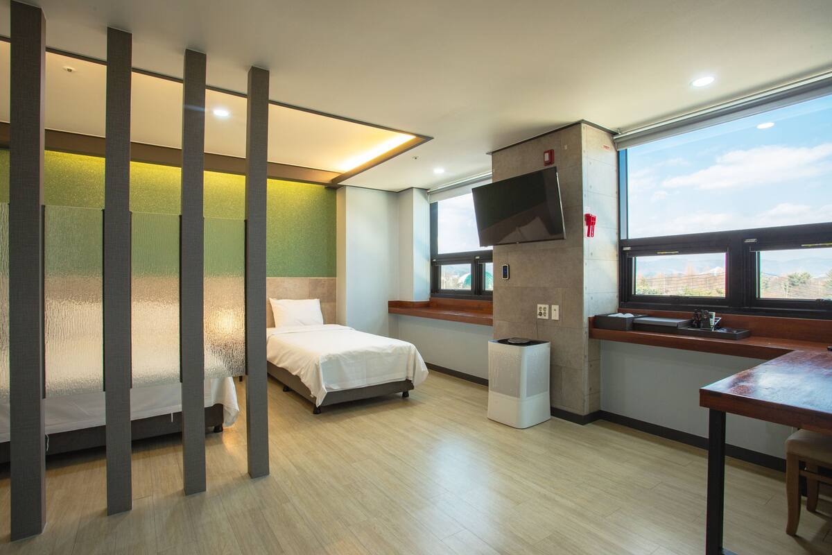 Quarto de hotel com cama, escrivaninha, televisão e janela com vista para a cidade.