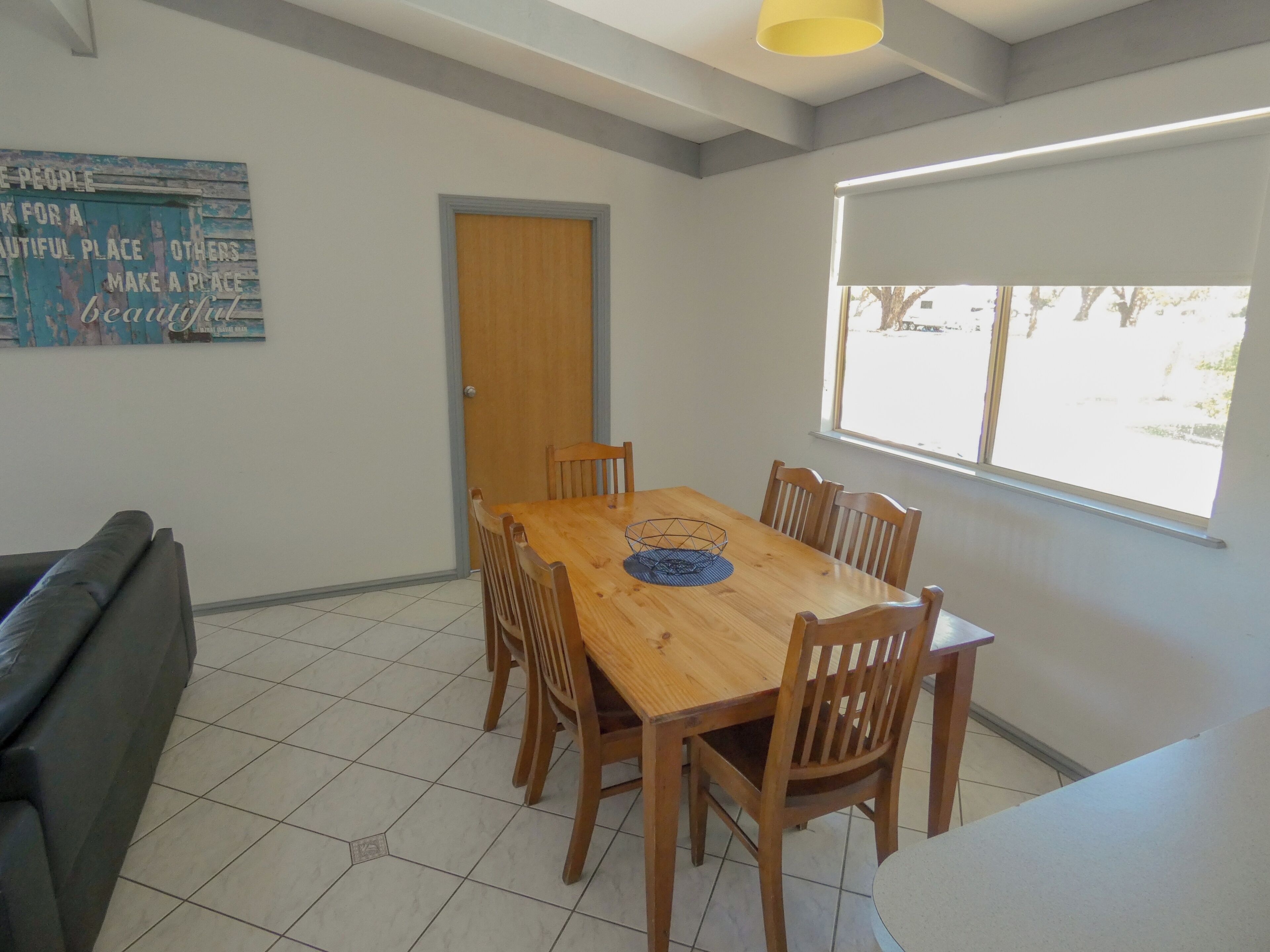 Uma sala de jantar com mesa e cadeiras de madeira, um sofá preto, uma porta e uma janela com vista.