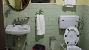 Casa de banho com lavatório, espelho, sanita e um caixote do lixo vermelho.