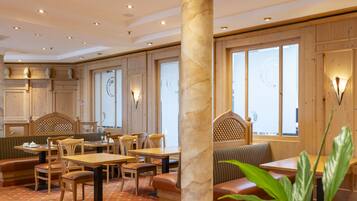 Um restaurante com painéis de madeira, diversas áreas de estar incluindo cabines e mesas, e grandes janelas com painéis de vidro decorativos.