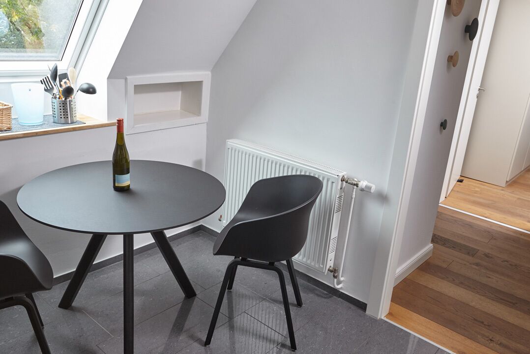 Uma cozinha moderna com uma mesa redonda, duas cadeiras pretas, uma garrafa de vinho e uma janela com vista.