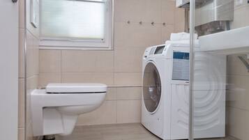 Casa de banho moderna com sanita, máquina de lavar roupa e janela com persianas.