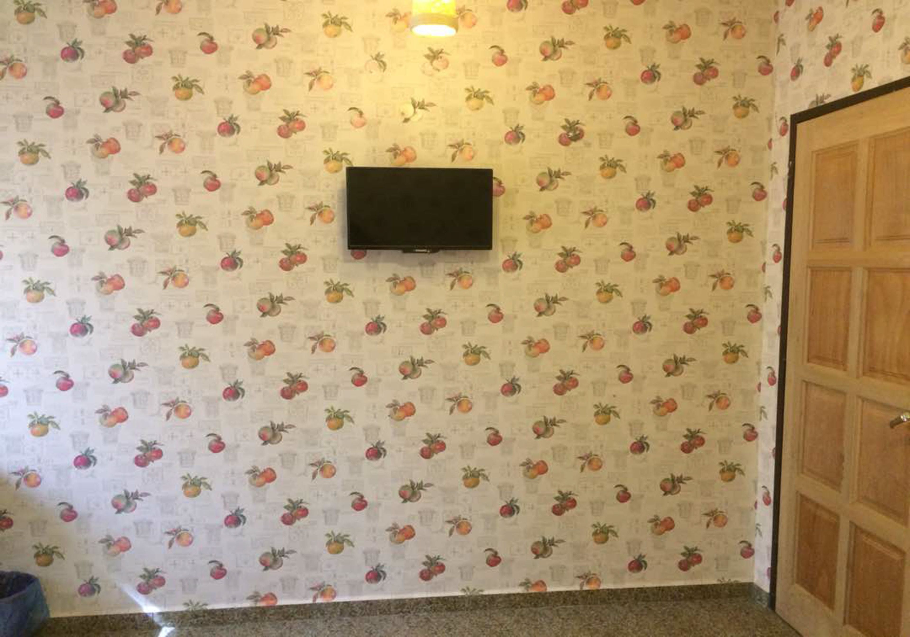Quarto com papel de parede estampado, televisão de tela plana na parede e porta de madeira.