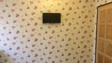 Quarto com papel de parede estampado, televisão de tela plana na parede e porta de madeira.