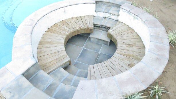 Escadaria de pedra circular que leva a uma área de hidromassagem, com uma piscina ao fundo.