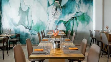 Uma área de jantar moderna com uma mesa longa posta para refeição, rodeada por cadeiras, e um grande mural abstrato na parede.