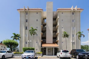 Um hotel de vários andares com uma torre central, varandas e um estacionamento com carros.