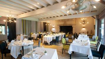 Restaurante com várias mesas redondas preparadas para refeições, lareira e lustres.