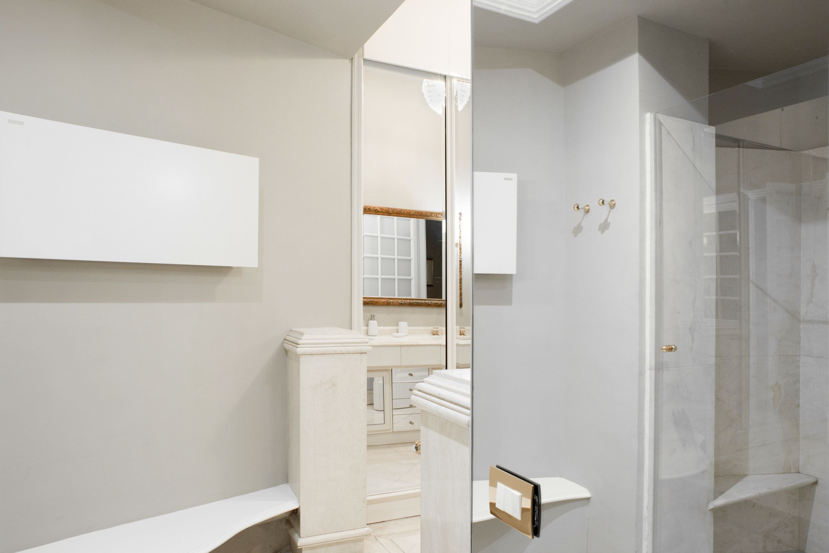 Uma casa de banho moderna com uma toucador branco, uma cabine de duche em vidro e chão em mosaico de mármore.