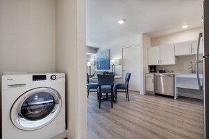 Cozinha compacta e moderna, com máquina de lavar embutida, sala de jantar com cadeiras e uma mesa pequena.