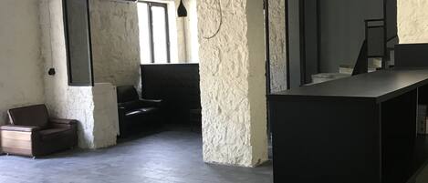 Uma sala de estar integrada com uma ilha de cozinha, um sofá e uma mesa de centro. Há luminárias pendentes e uma parede texturizada.
