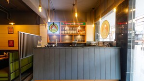 Uma área de bar com balcão, prateleiras com garrafas e uma placa com a inscrição 'Loupis Sagar'.