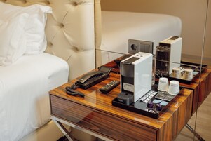 Quarto de hotel com uma cama, uma escrivaninha de madeira com telefone, uma cafeteira e um pequeno alto-falante.