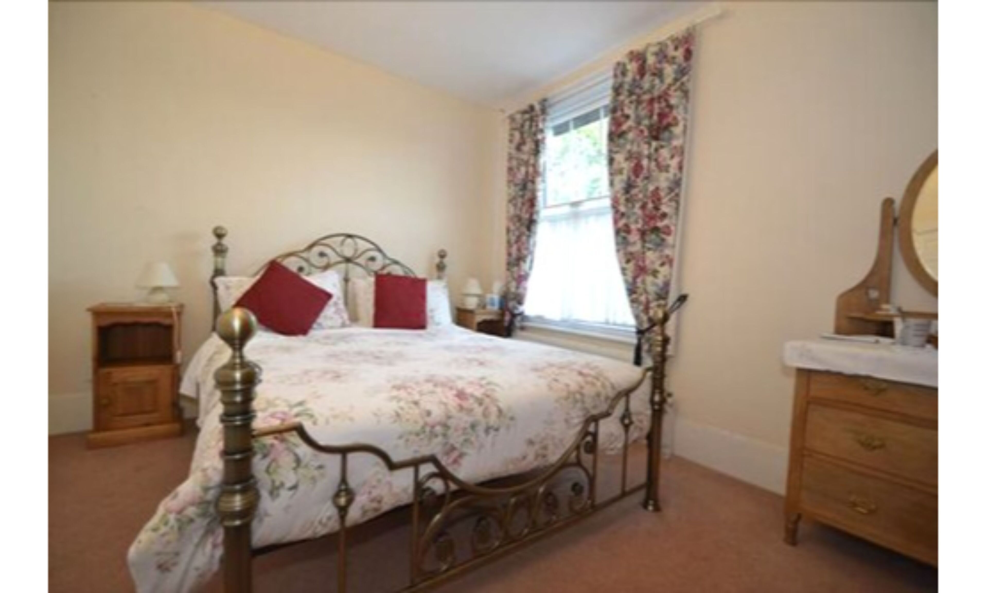 Um quarto com cama de dossel, mesa de cabeceira de madeira, cômoda e janela com cortinas florais.