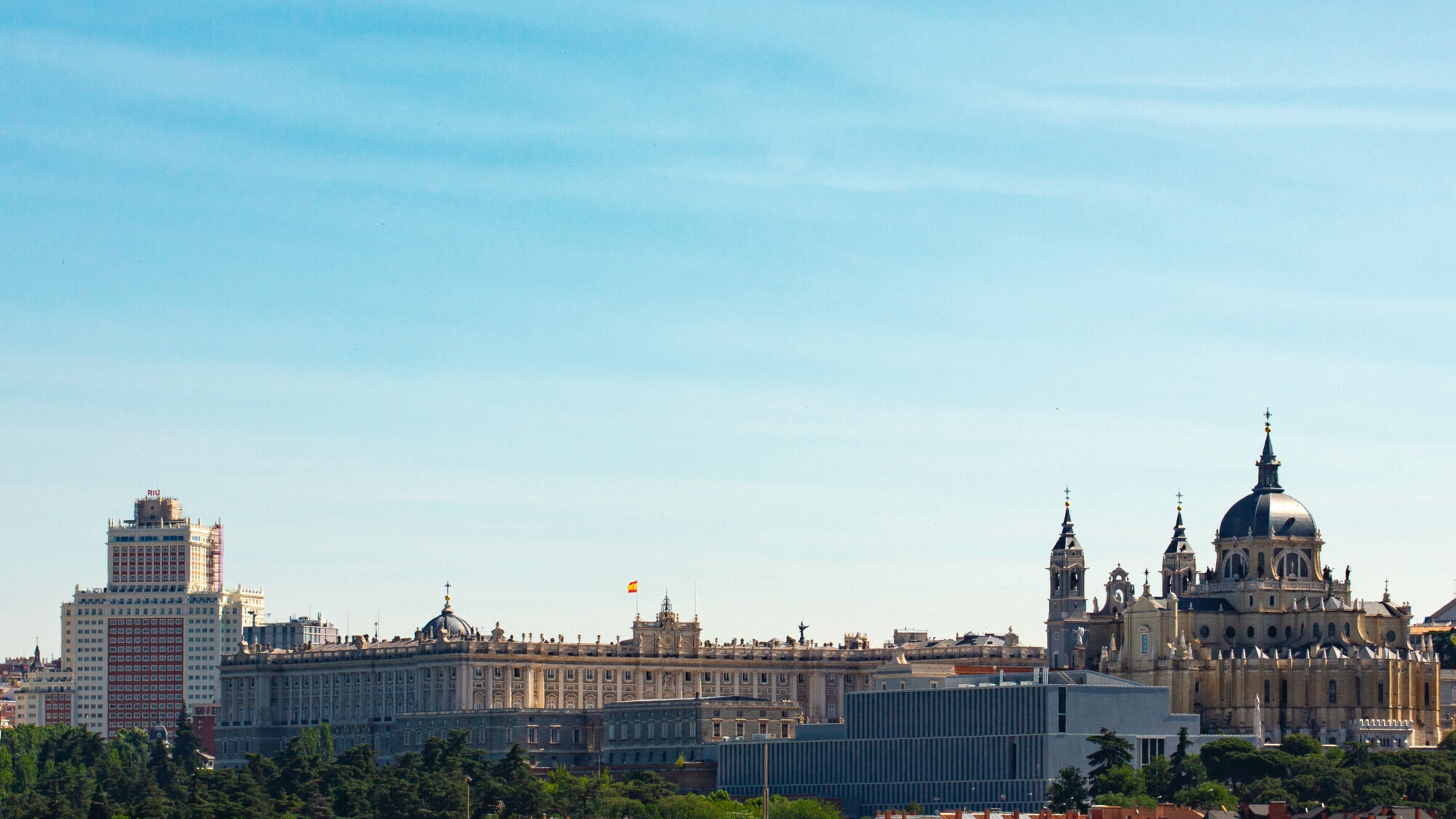 Um edifício histórico grande com várias cúpulas e torres, rodeado por outros edifícios e árvores.