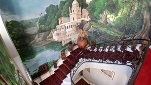 Escada com tapete vermelho e um mural de um edifício na parede.