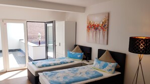 Quarto moderno com duas camas, porta de vidro deslizante para uma varanda, um quadro na parede e um abajur.