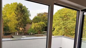 Um edifício moderno com grandes janelas que oferecem vista para um parque arborizado e um edifício de tijolos.