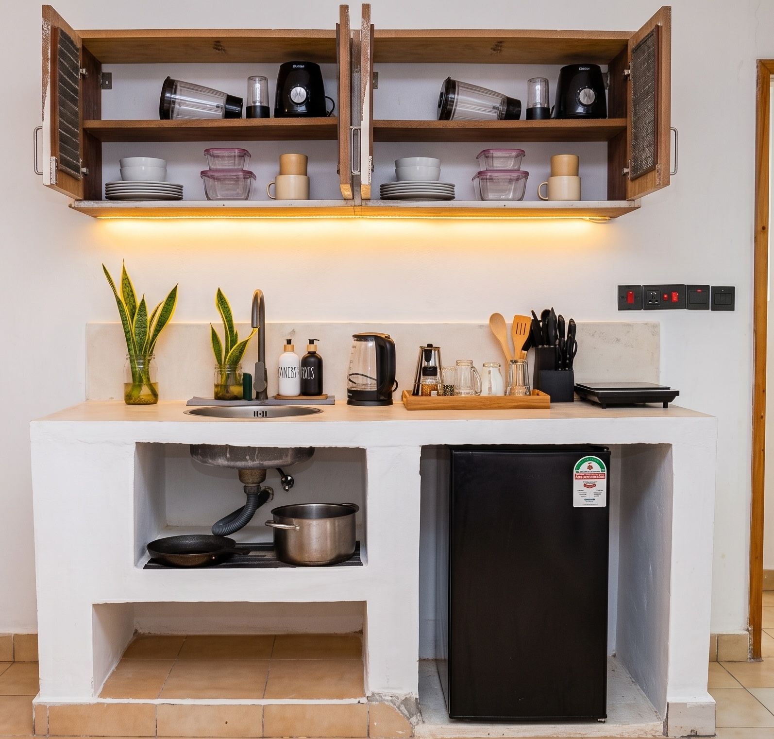 Cozinha compacta com geladeira embutida, pia e bancada com diversos eletrodomésticos e utensílios.