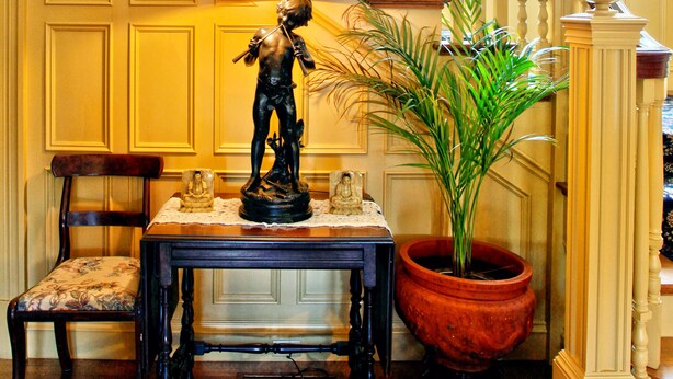 Uma escadaria com corrimão de madeira, uma mesa com uma estátua, uma cadeira e um vaso de planta.