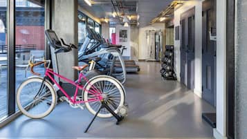 Uma academia com equipamentos de exercício, uma bicicleta rosa e vista para o exterior.