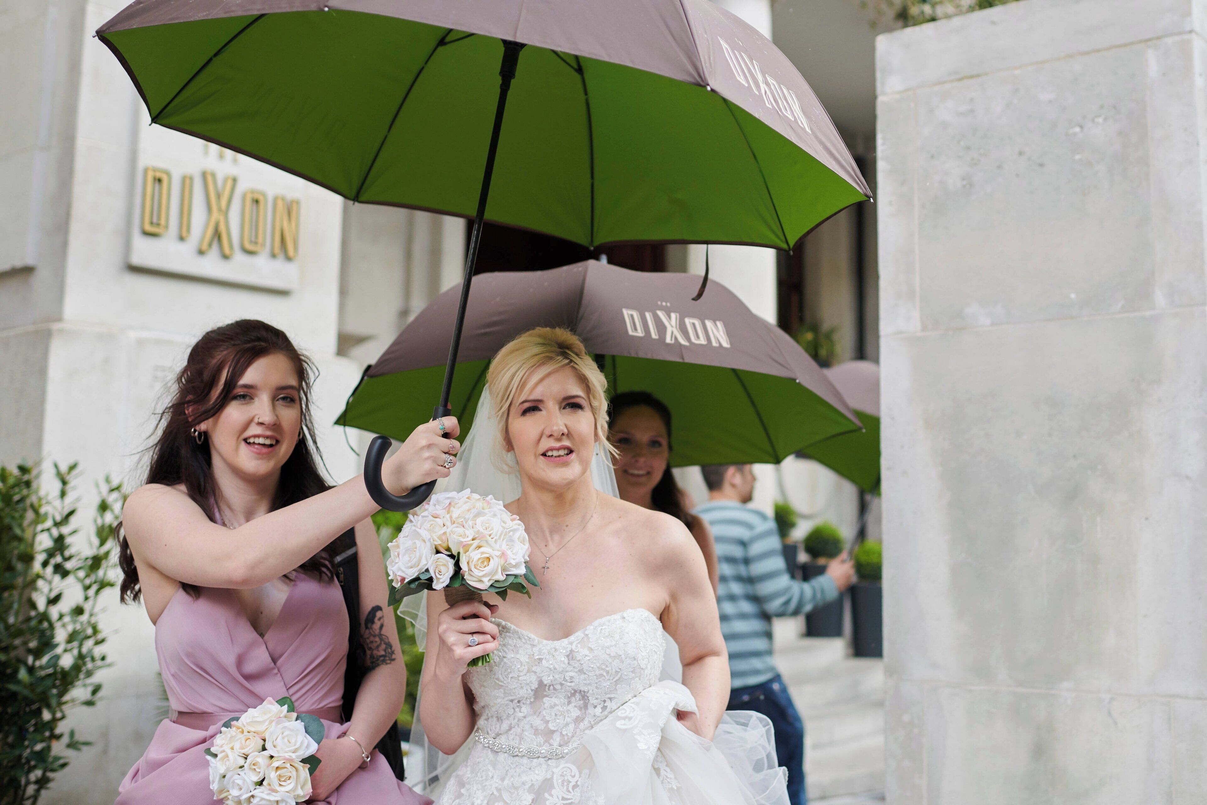 Cena de casamento com uma noiva e damas de honra debaixo de um guarda-chuva.