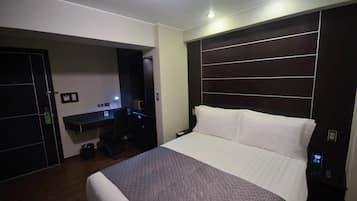 Quarto de hotel com uma cama grande, uma escrivaninha com computador e um guarda-roupa.
