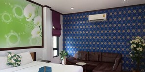Quarto de hotel com uma cama grande, um sofá marrom, ar condicionado na parede e uma janela com vista.