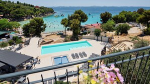 Uma área de piscina com vista para o mar, cercada por árvores e edifícios.