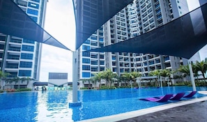 Área de piscina com projeto arquitetônico moderno, rodeada por edifícios altos e palmeiras.